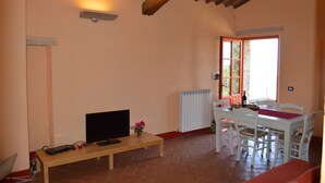 Uma sala de estar com televisão, mesa de madeira e espaço para refeições com cadeiras.