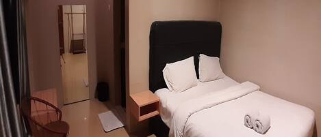Quarto de hotel com uma cama, mesa de cabeceira, cadeira e pequena mesa com abajur.