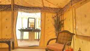 Quarto com cadeira tradicional, mesa de vidro com bebidas e vista para um banheiro com pia e espelho.