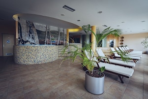 Um hall com parede em mosaico, balcão de recepção e espreguiçadeiras.