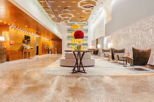 Um hall moderno com piso de mármore, uma mesa redonda central com um vaso de flores vermelhas e uma área de estar com poltronas confortáveis.