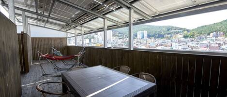 Um pátio externo com mesa e cadeiras, com vista para um horizonte urbano com edifícios e colinas.