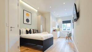 Um quarto moderno com cama, mesa de cabeceira e televisão fixada na parede.
