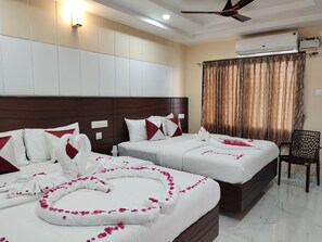 Quarto de hotel com duas camas, um ventilador de teto, um ar condicionado e uma cadeira.