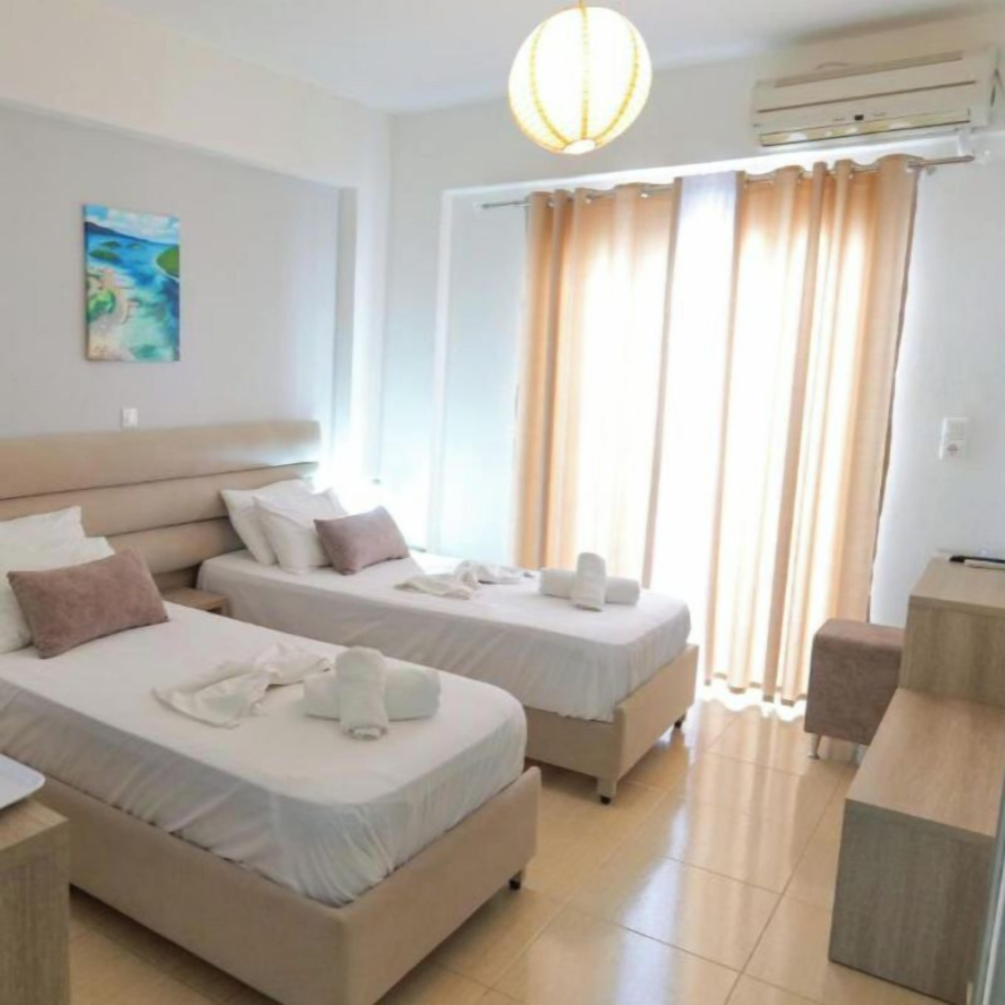 Quarto de hotel com duas camas, um quadro na parede, um aparelho de ar condicionado e vista para o exterior pela janela.