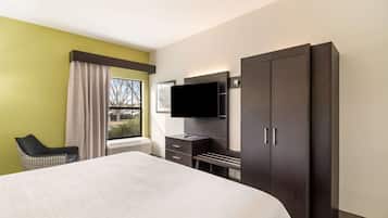 Quarto de hotel com cama, televisão na parede, guarda-roupa, secretária com cadeira e janela com cortinas.
