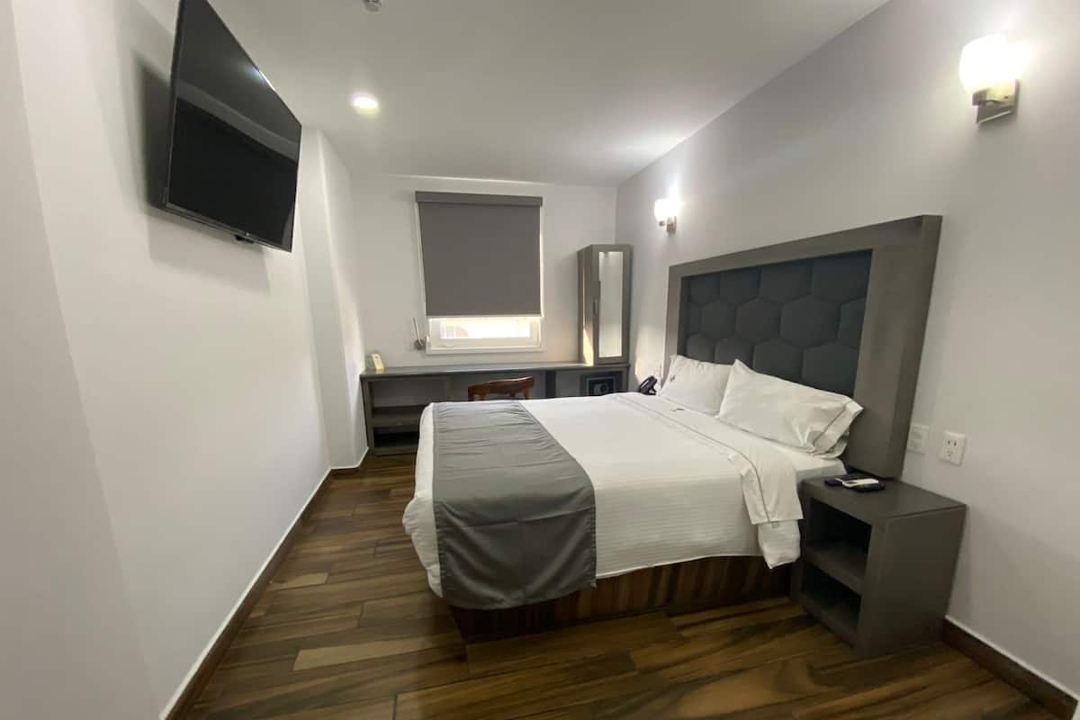 Quarto de hotel moderno com uma cama grande, uma escrivaninha, televisão de tela plana e janela com persianas.