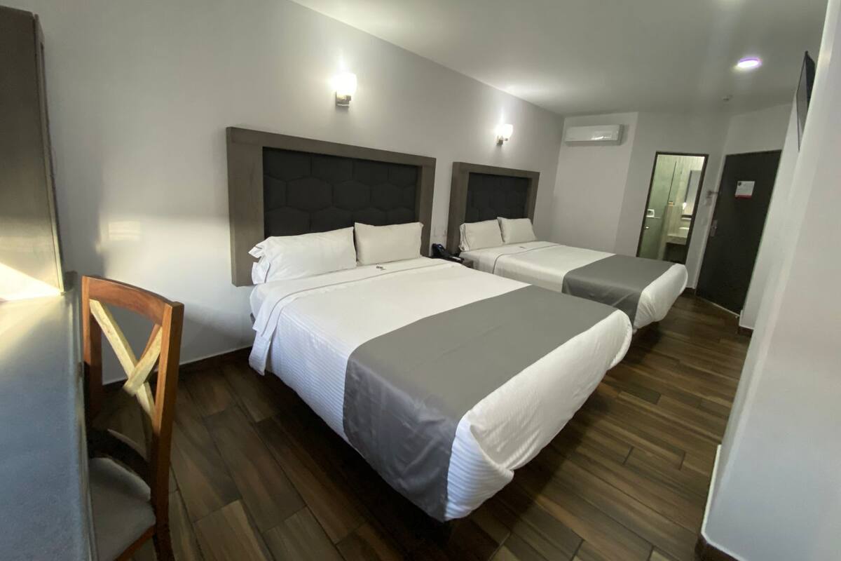 Quarto de hotel com duas camas, uma cadeira de madeira e um espelho.