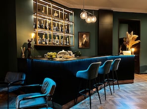 Uma área de bar com balcão azul, vários bancos altos e uma variedade de garrafas e copos.
