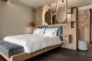 Quarto moderno com cama grande, cabeceira de madeira, guarda-roupa embutido e um espelho redondo.