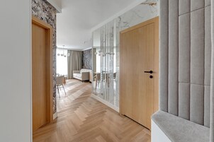 Um interior moderno com piso de madeira, área de estar com sofá e cadeiras, e uma divisória de vidro.
