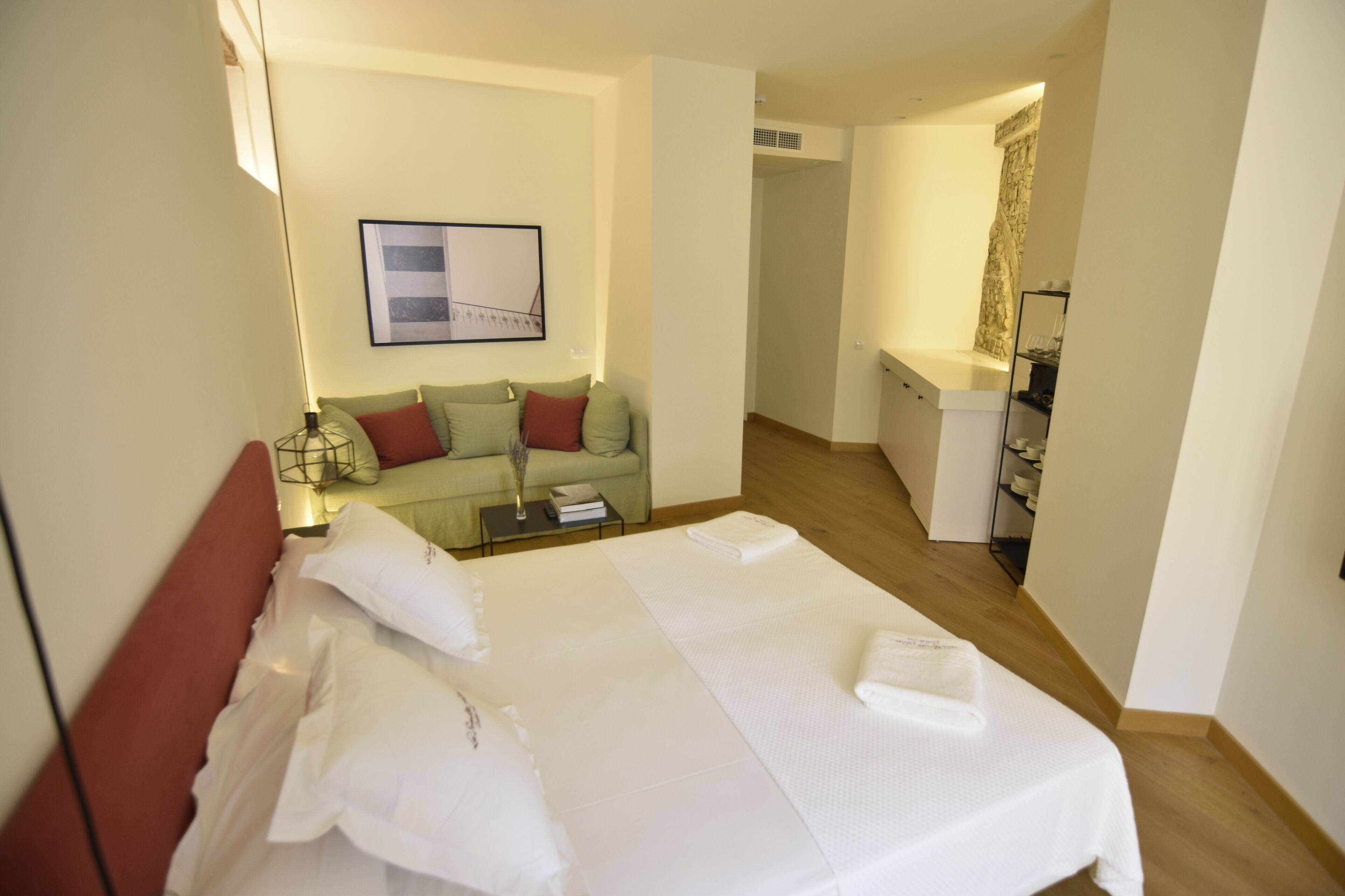 Quarto de hotel com cama, sofá, uma mesinha com abajur e um quadro na parede.