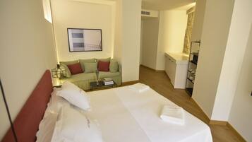 Quarto de hotel com cama, sofá, uma mesinha com abajur e um quadro na parede.