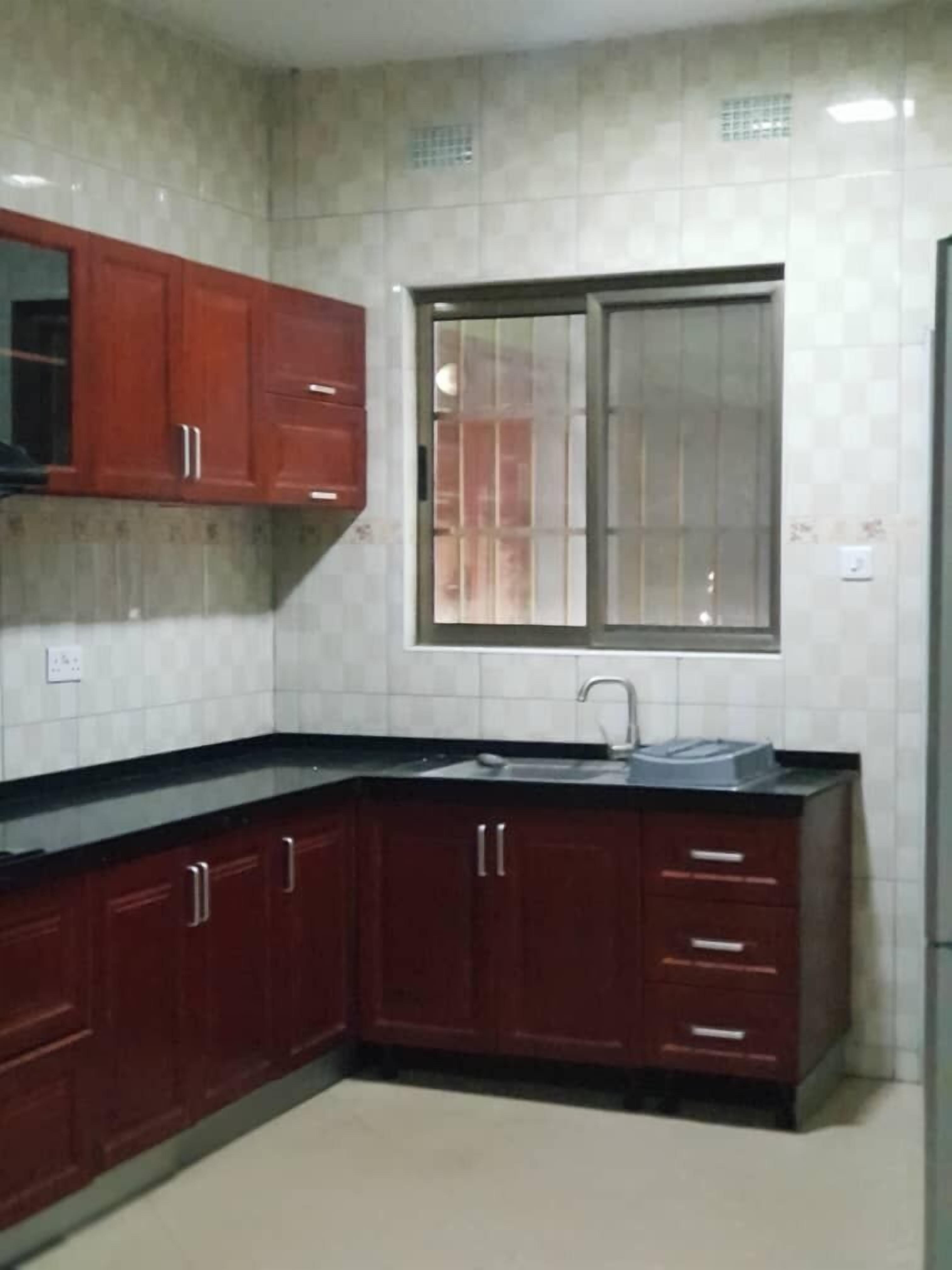 Uma cozinha com armários de madeira escura, bancada preta e janela com grades de metal.