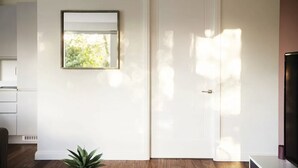 Quarto com porta branca, quadro pendurado na parede e planta no chão.