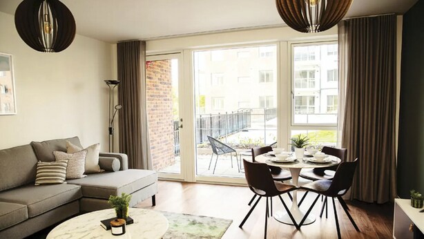 Uma sala de estar moderna com um sofá, uma mesa de jantar com cadeiras, uma mesa de centro e uma grande porta de vidro deslizante que dá para uma varanda.