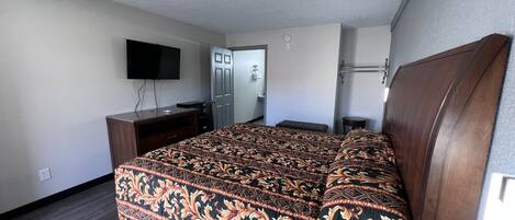 Quarto de hotel com cama, escrivaninha, televisão, guarda-roupa e porta do banheiro.