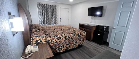 Quarto de hotel com cama, escrivaninha com telefone, televisão na parede, micro-ondas e frigorífico.