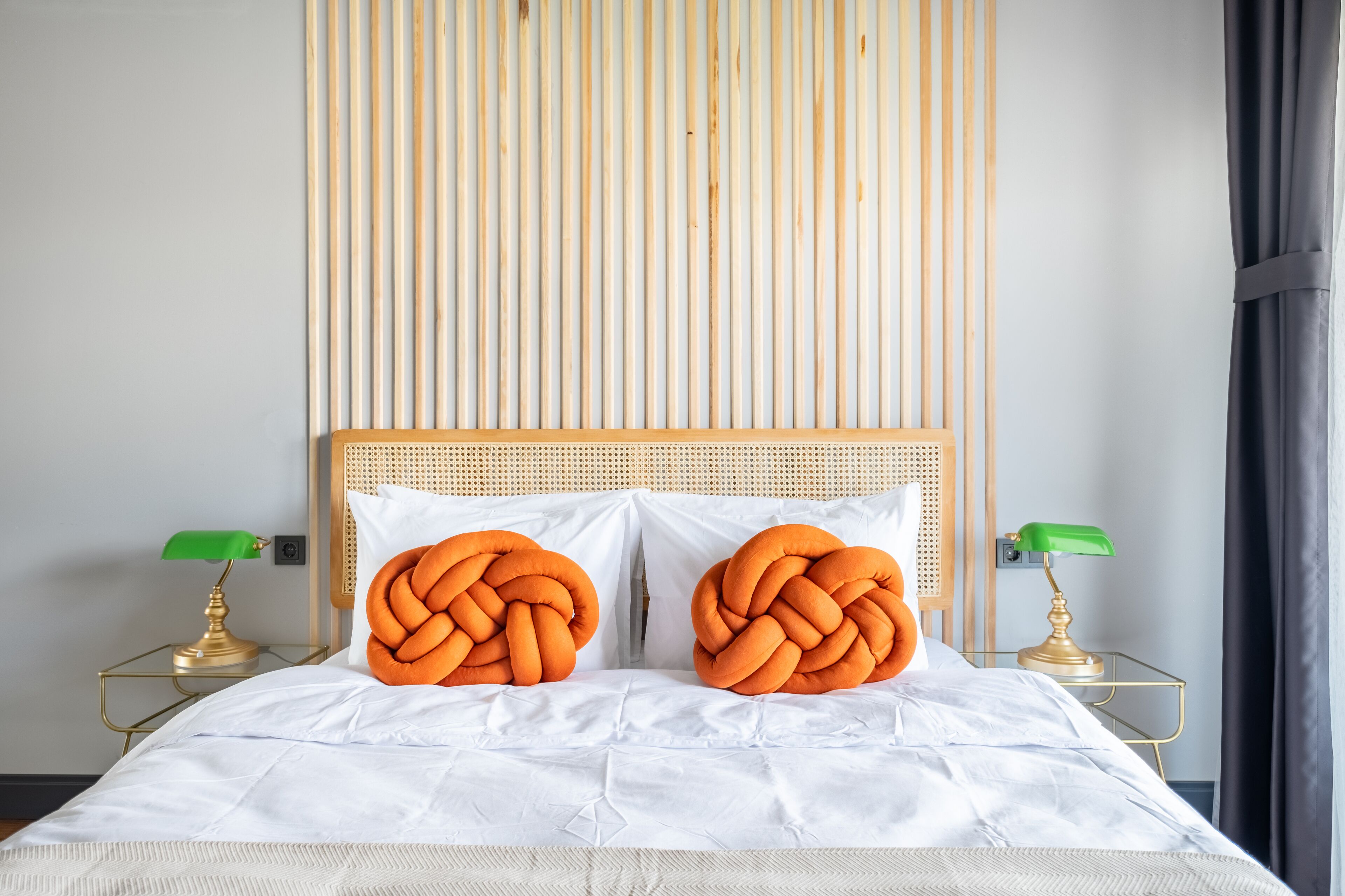 Uma cama bem arrumada com roupa de cama branca, dois travesseiros de nó laranja e uma cabeceira de madeira.