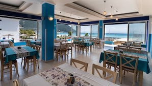 Um restaurante com mesas e cadeiras, grandes janelas com vista para o mar, e uma decoração azul e branca.