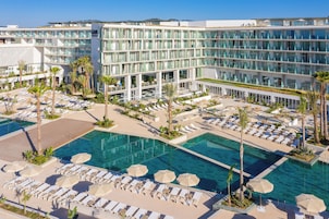 Um hotel com várias piscinas, espreguiçadeiras e palmeiras.