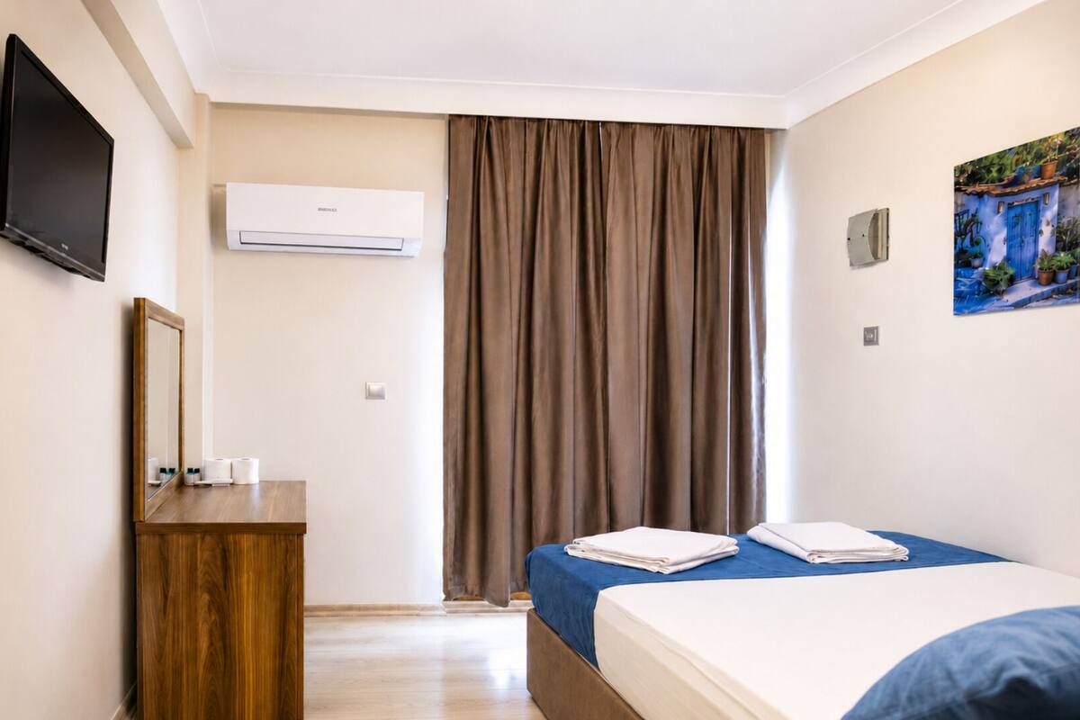 Quarto de hotel com cama, escrivaninha, televisão de tela plana, ar condicionado e um quadro na parede.