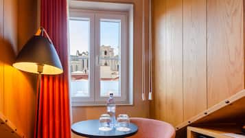 Quarto com parede de madeira, janela com vista para um prédio, mesa com luminária e uma cadeira.