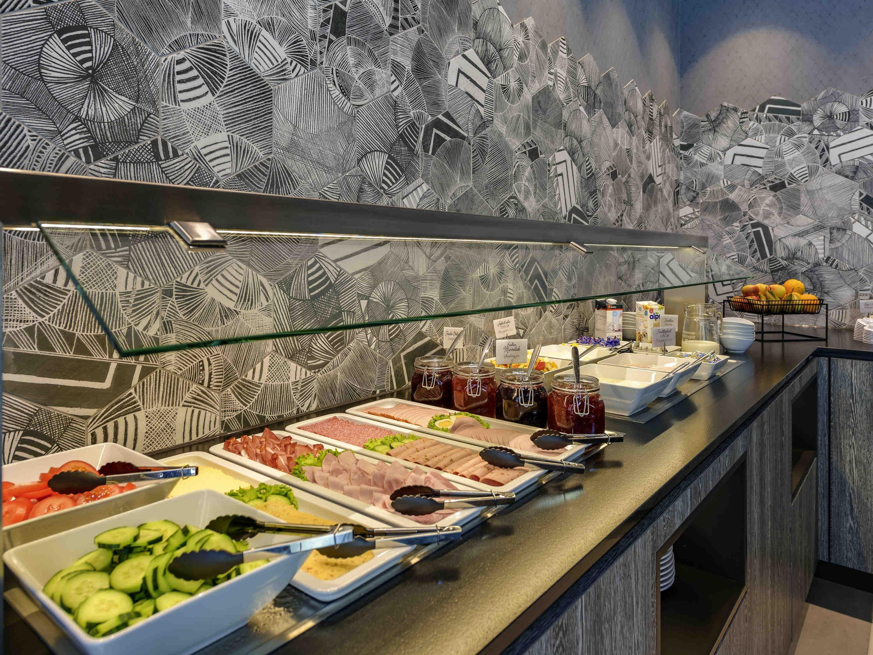 Buffet com diversos tipos de comida, incluindo carnes, vegetais e acompanhamentos, com um papel de parede estampado ao fundo.