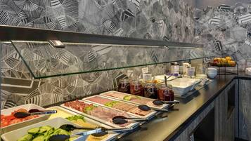 Buffet com diversos tipos de comida, incluindo carnes, vegetais e acompanhamentos, com um papel de parede estampado ao fundo.