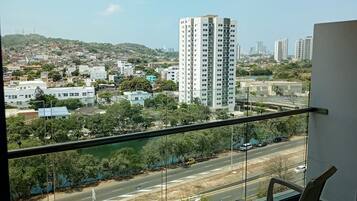 Uma varanda com vista para a paisagem urbana, incluindo edifícios altos e um rio. Há duas cadeiras e uma mesa na varanda.
