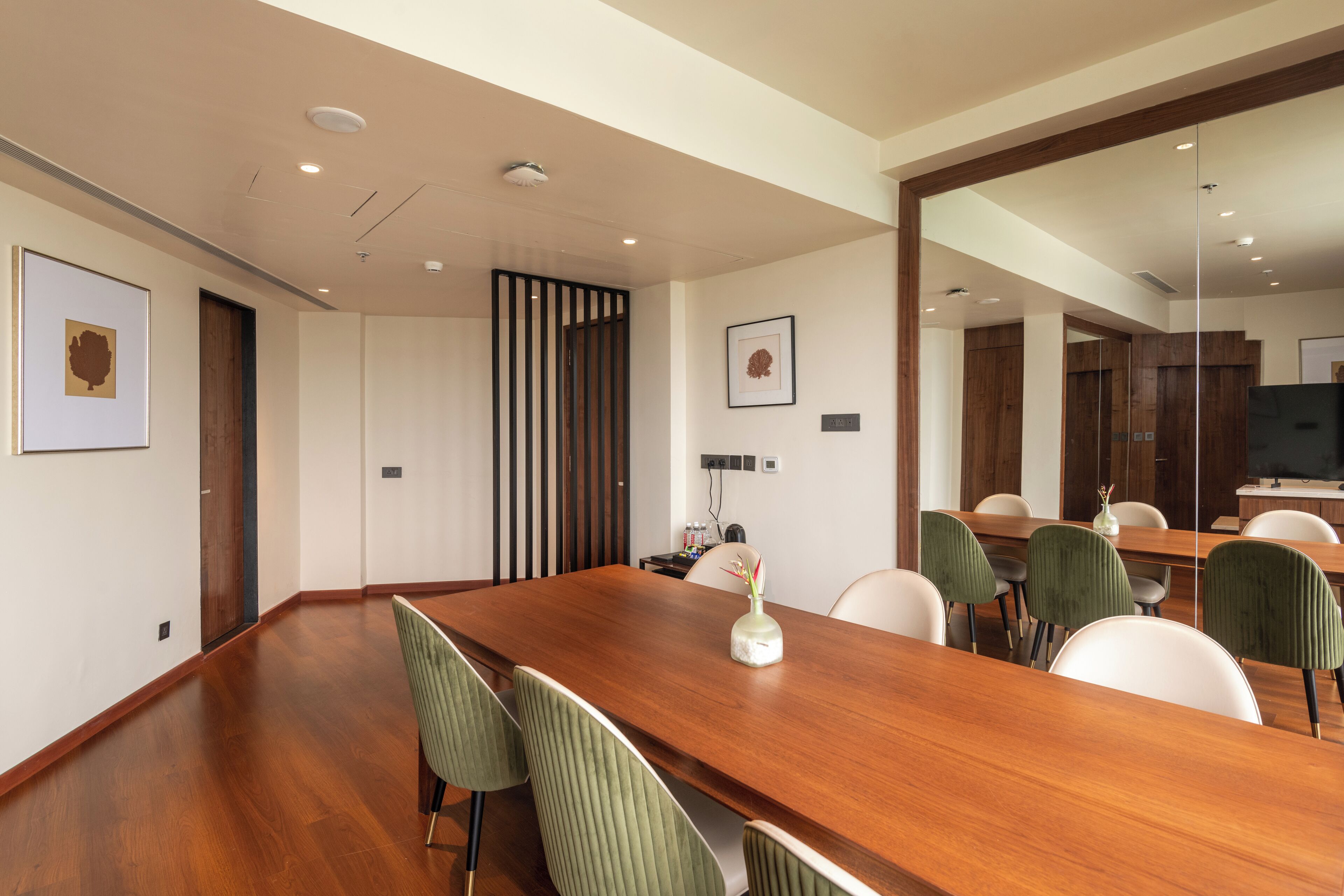 Uma sala de conferências moderna com uma longa mesa de madeira, cadeiras estofadas em verde e um espelho grande na parede.