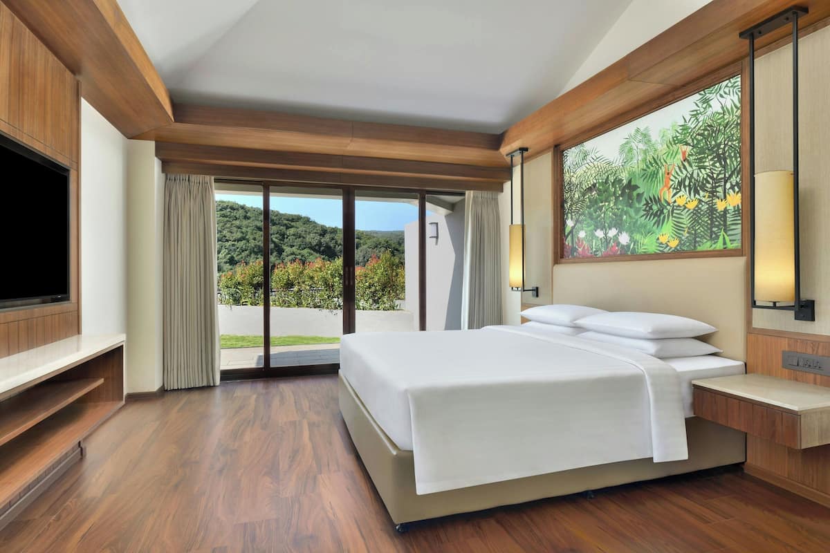 Quarto de hotel moderno com uma cama grande, televisão de tela plana, piso de madeira e varanda com vista para área verde.