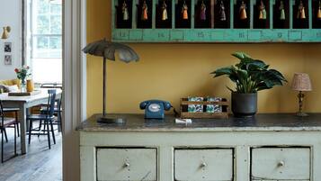Quarto em estilo vintage com um aparador de madeira exibindo compartimentos numerados, um telefone de discagem azul, uma planta em vaso e uma luminária sobre uma mesa de madeira.