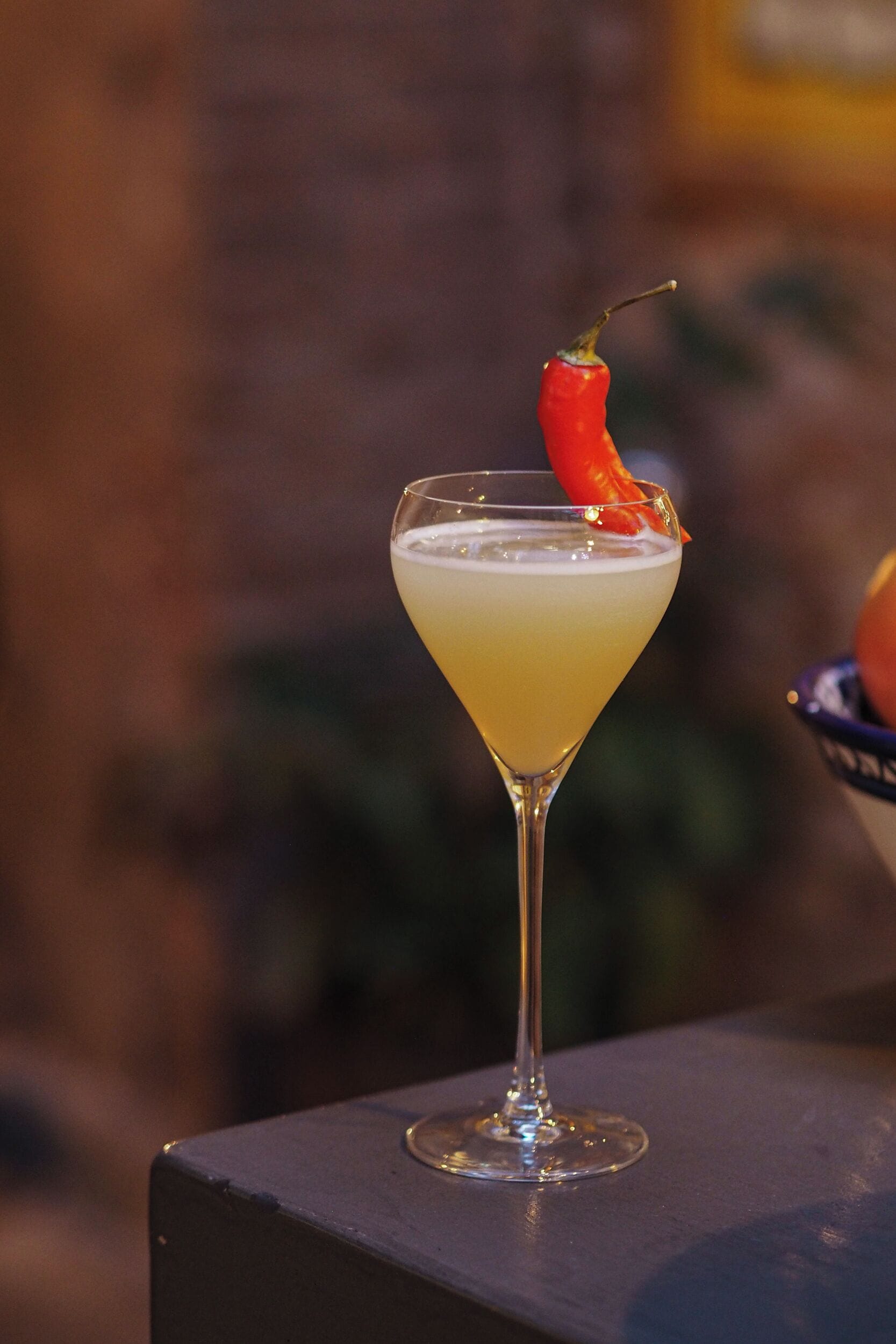 Um coquetel em copo de martini com um pimentão vermelho como enfeite em um balcão de bar.
