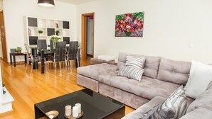 Uma sala de estar moderna com um sofá cinzento, uma mesa de centro preta e uma área de jantar com uma mesa e cadeiras de vidro.