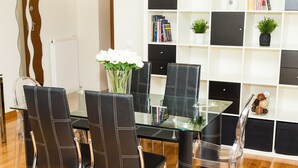 Uma área de refeições com mesa de vidro e cadeiras, um vaso de flores e uma estante com livros e objetos decorativos.