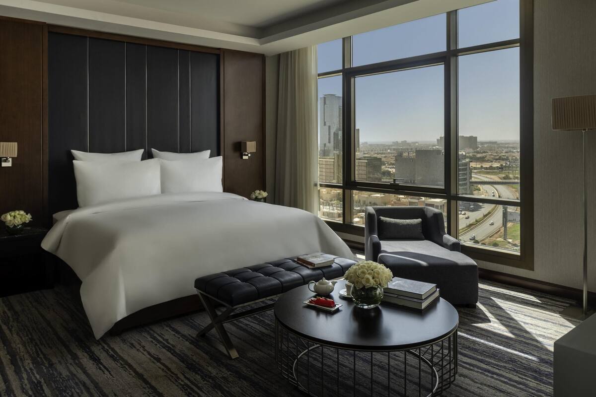 Quarto de hotel moderno com uma cama grande, área de estar e vista para a cidade.