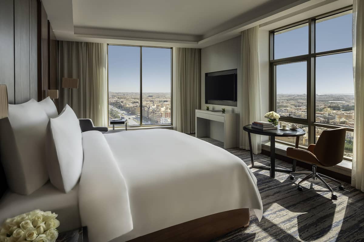 Quarto de hotel com uma cama grande, uma mesa, uma cadeira, uma televisão e vista para a cidade.