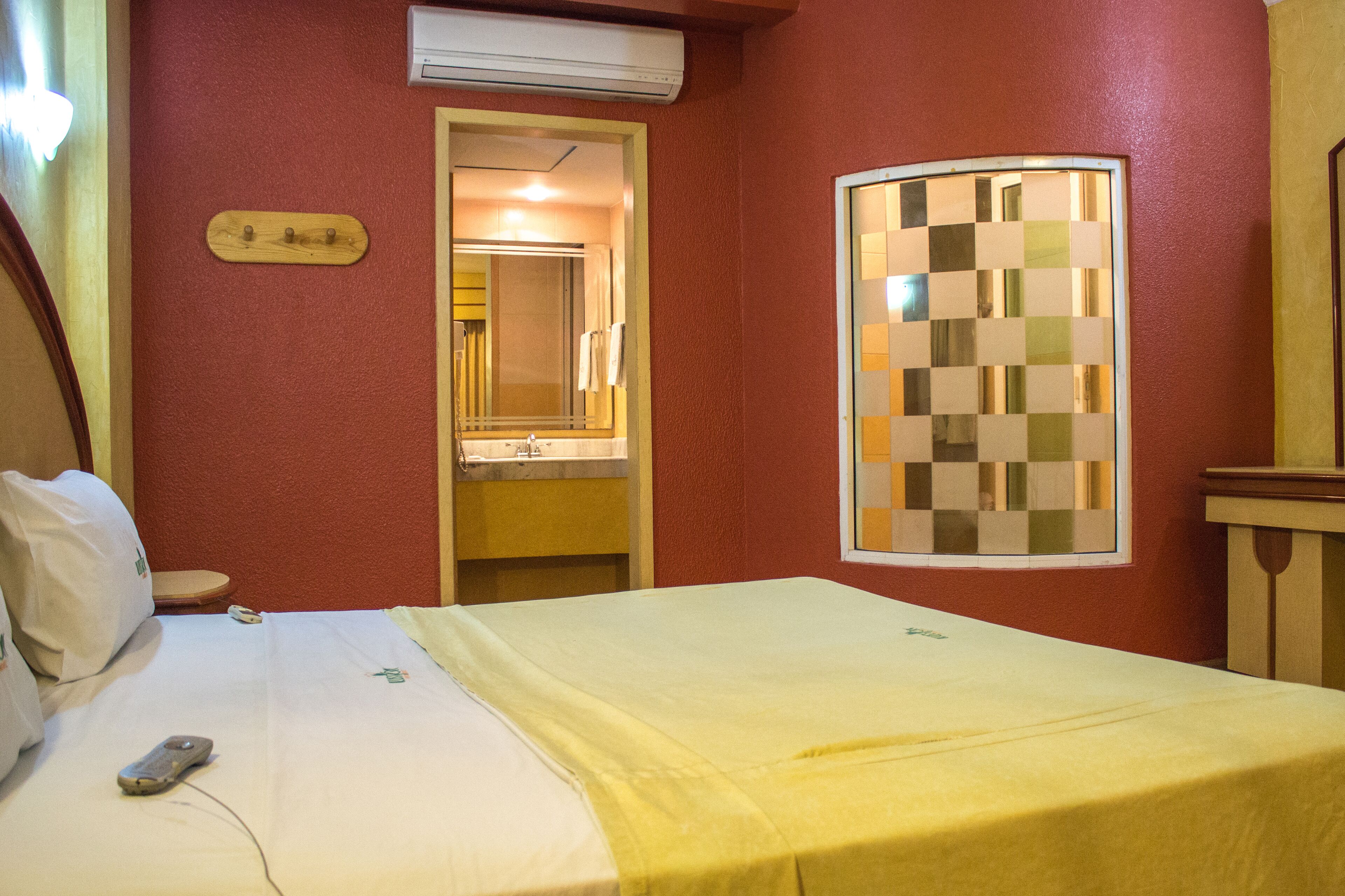 Quarto de hotel com uma cama, mesa de cabeceira, espelho e janela com padrão xadrez.