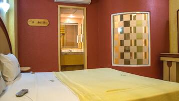 Quarto de hotel com uma cama, mesa de cabeceira, espelho e janela com padrão xadrez.