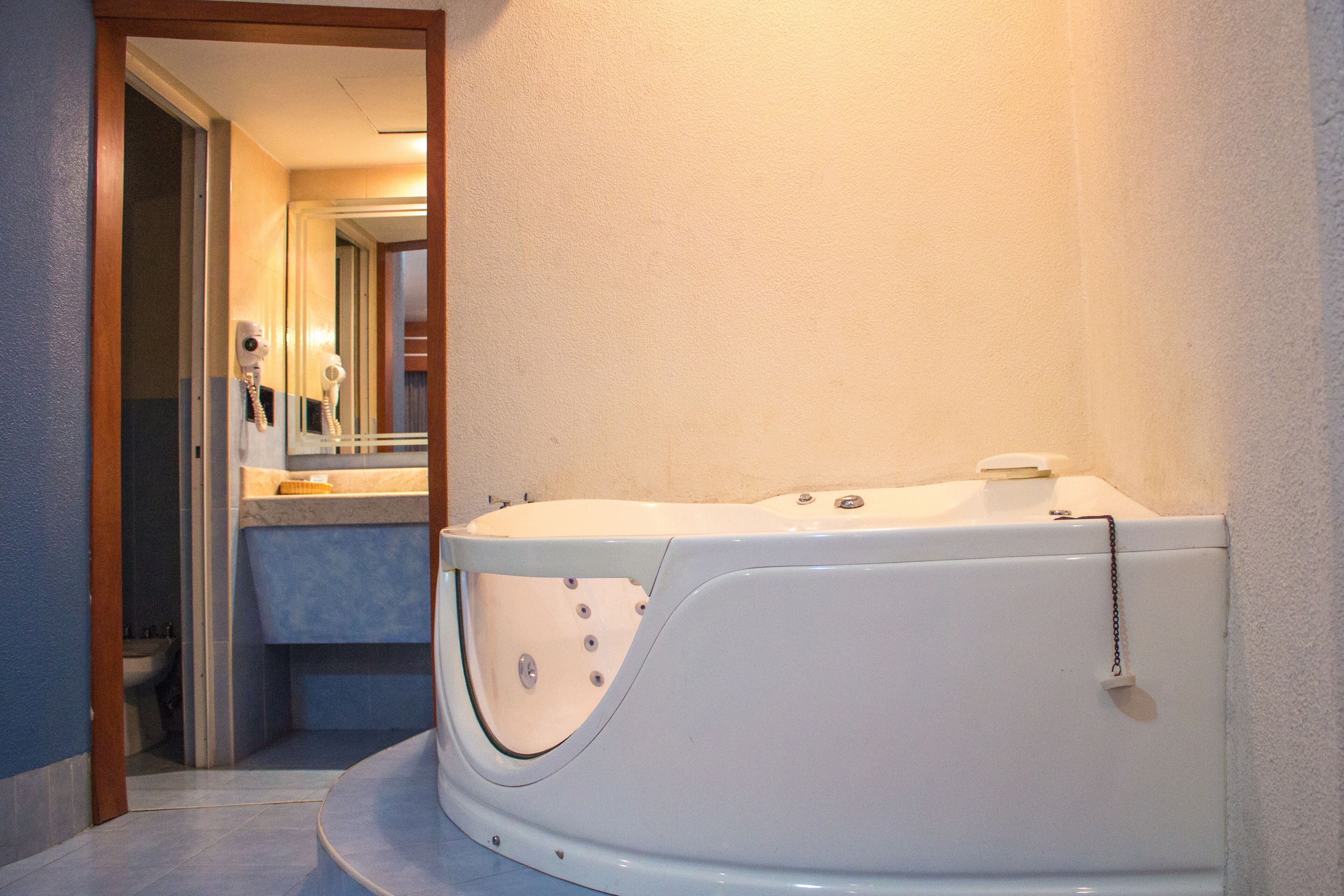 Uma casa de banho moderna com uma banheira curva, uma toucador com espelho e uma sanita visível através de uma porta aberta.