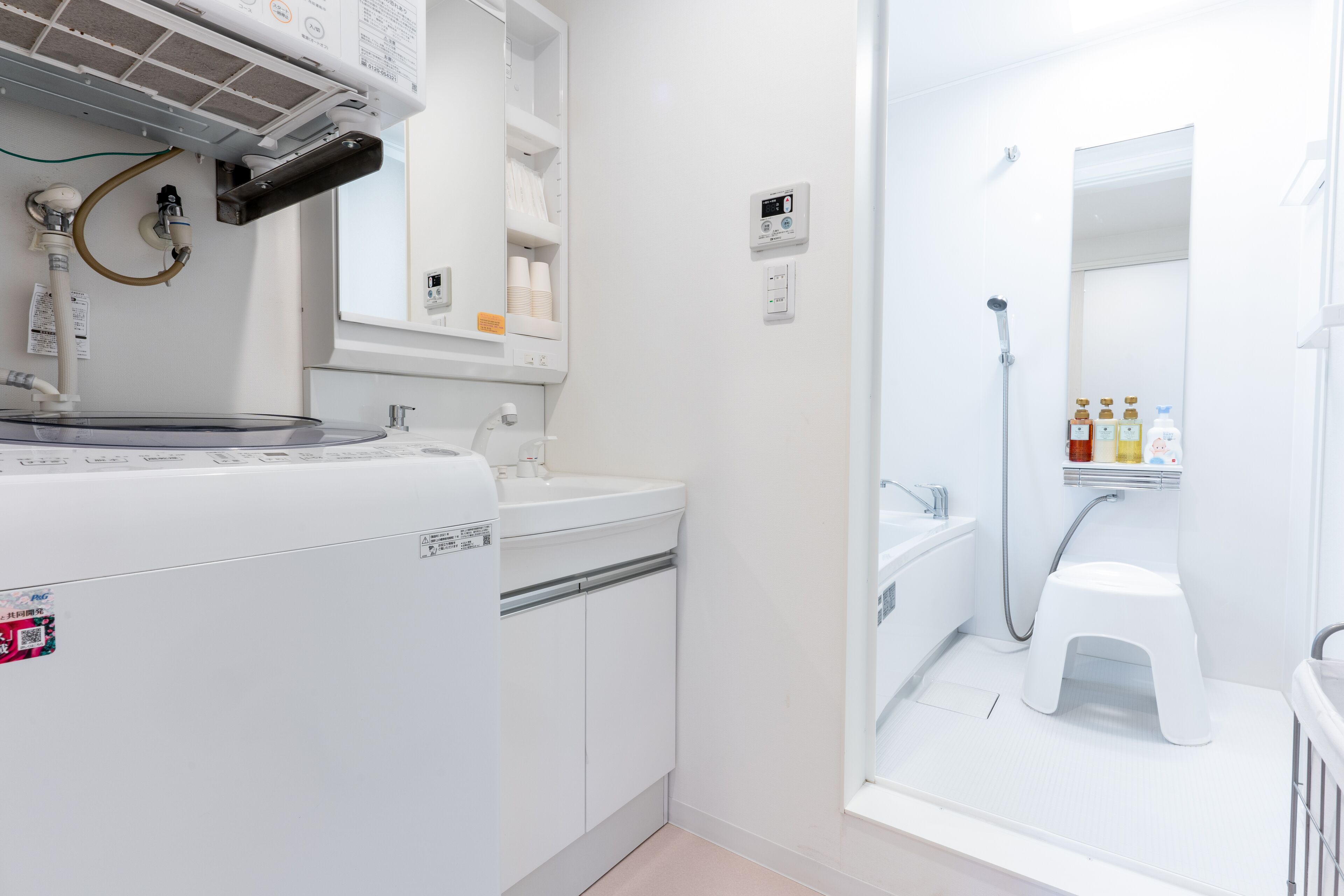 Uma casa de banho moderna com máquina de lavar roupa, lavatório, espelho e cabine de duche.