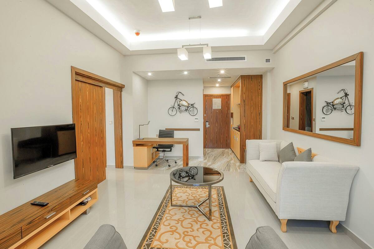Uma sala de estar moderna com uma TV de tela plana, um rack de madeira, um sofá, uma mesa de centro e um tapete estampado.