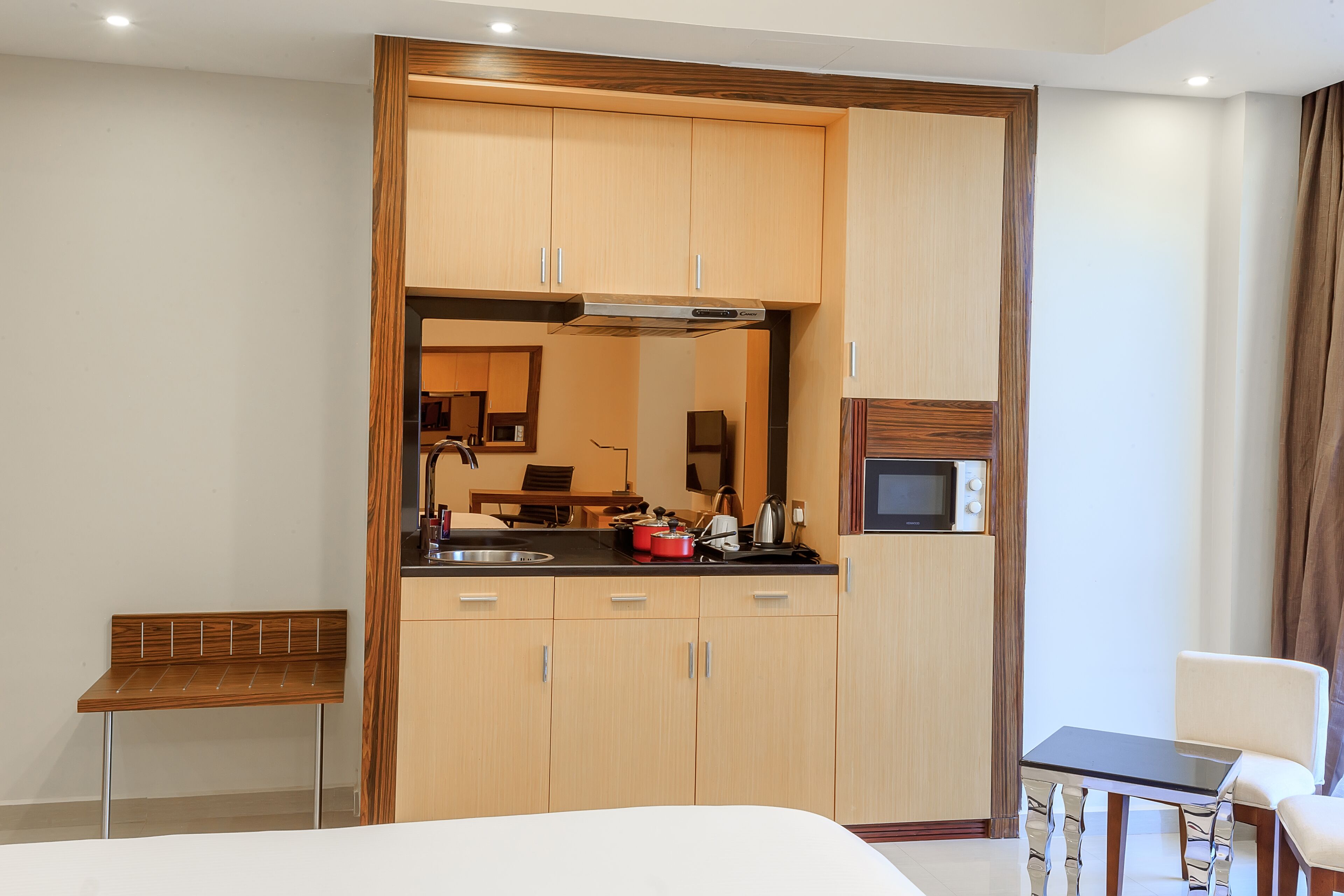 Quarto de hotel moderno com cozinha compacta, cama, mesa pequena e uma cadeira.