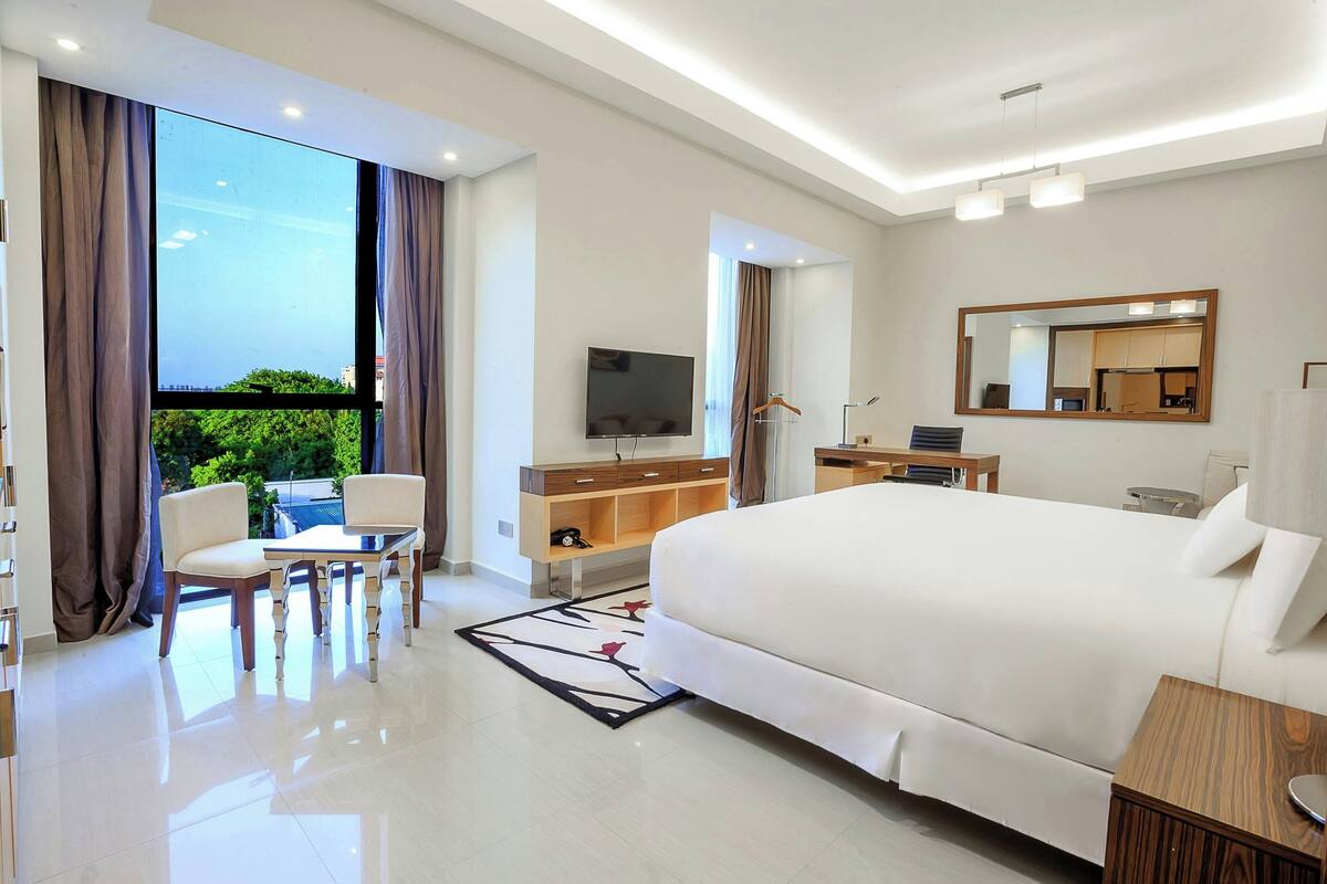 Quarto de hotel moderno com uma cama grande, televisão, escrivaninha e vista para o exterior.