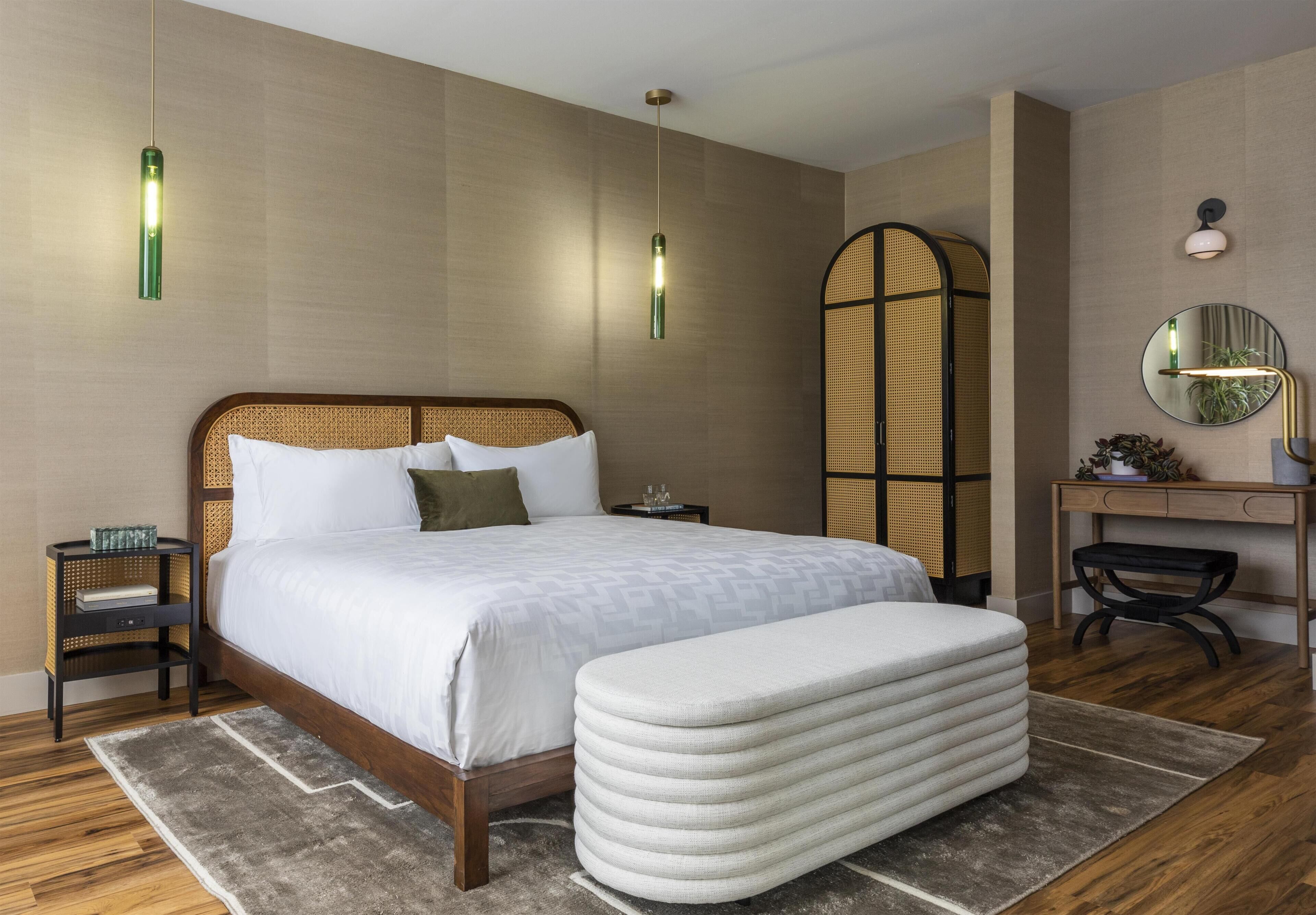 Quarto de hotel moderno com cama de madeira, espelho redondo, escrivaninha e divisória de vime.