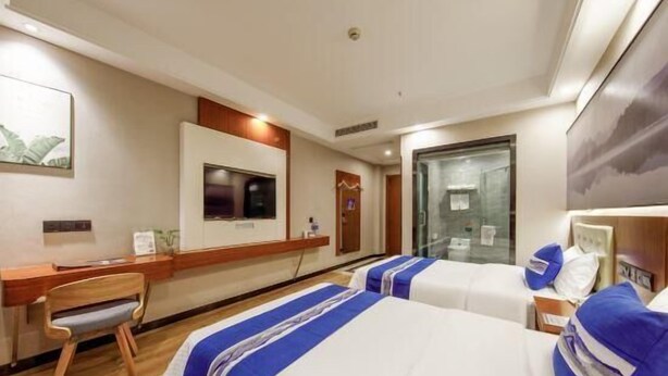 Quarto de hotel com duas camas, uma escrivaninha, uma cadeira, televisão e uma janela grande.