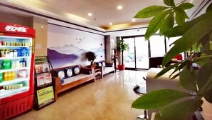 Um saguão de hotel com máquina de vendas automática, um mural, área de estar e uma janela grande.