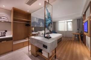 Quarto de hotel moderno com uma cama grande, banheiro separado com toucador, espelho amplo e televisão.