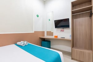 Quarto de hotel com cama, televisão, espelho, guarda-roupa e uma pequena mesa com uma garrafa e uma caixa.